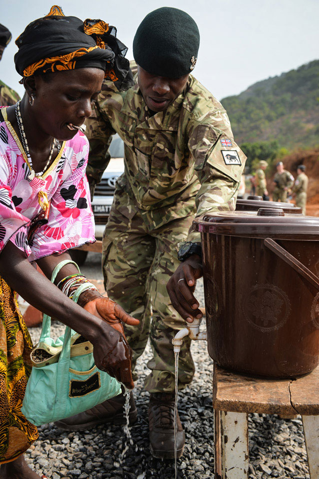 A member of The Rifles helping a woman use a mobile hand washing ...